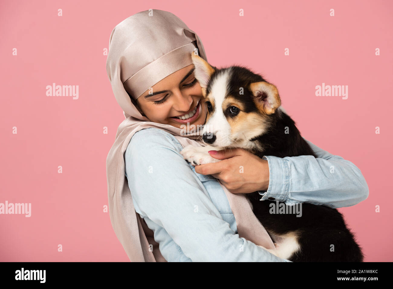 smiling arabic woman in hijab holding cute corgi puppy, isolated on ...