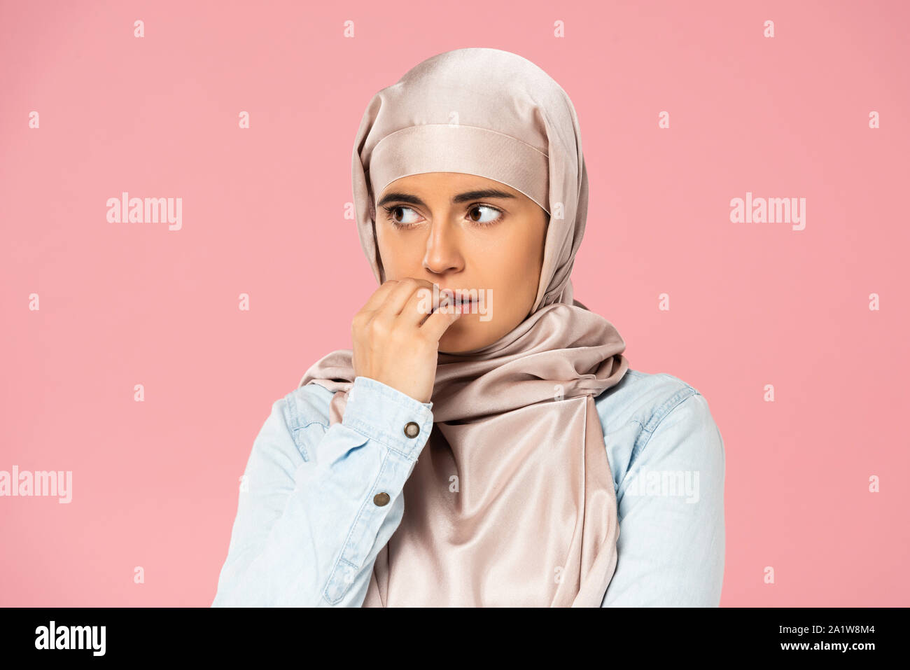 scared muslim girl in hijab biting nails, isolated on pink Stock Photo ...