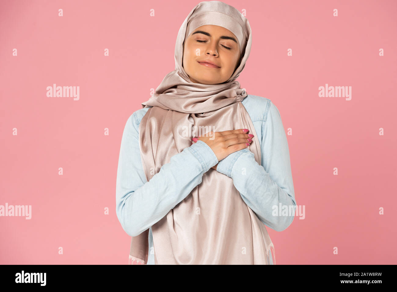 happy muslim girl holding hands on heart, isolated on pink Stock Photo ...