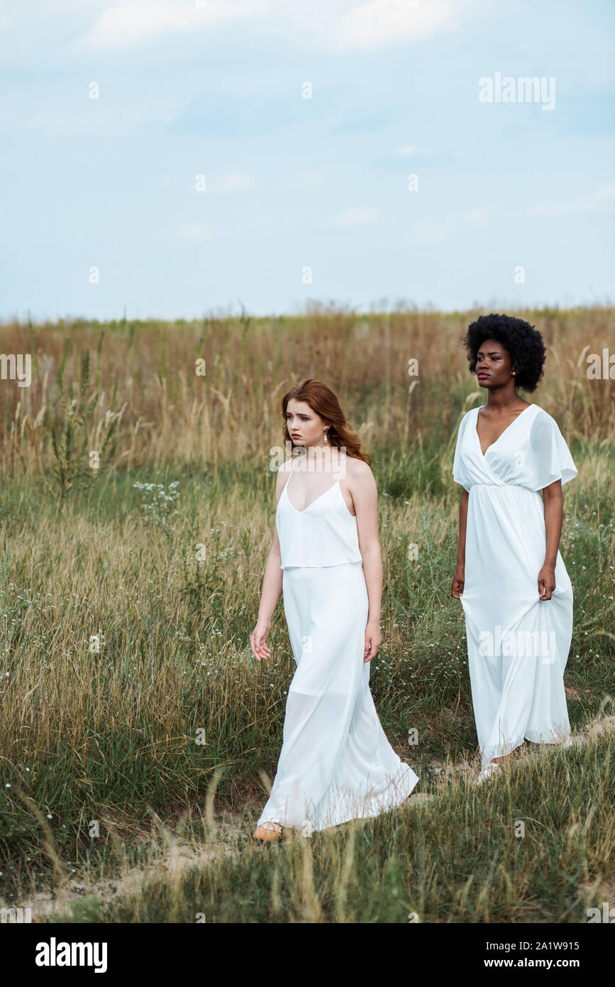 selective focus of attractive multicultural women walking on path near ...