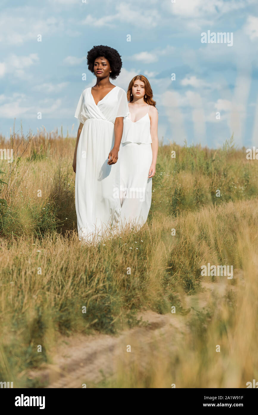 selective focus of attractive multicultural girls walking on path near ...