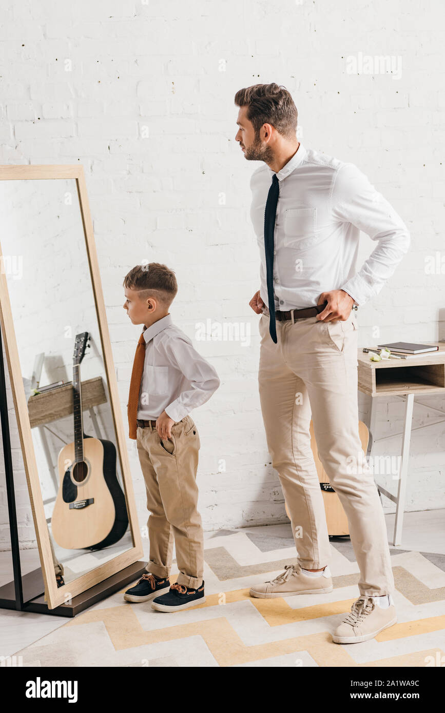 full length view of son and father in formal wear standing near mirror ...