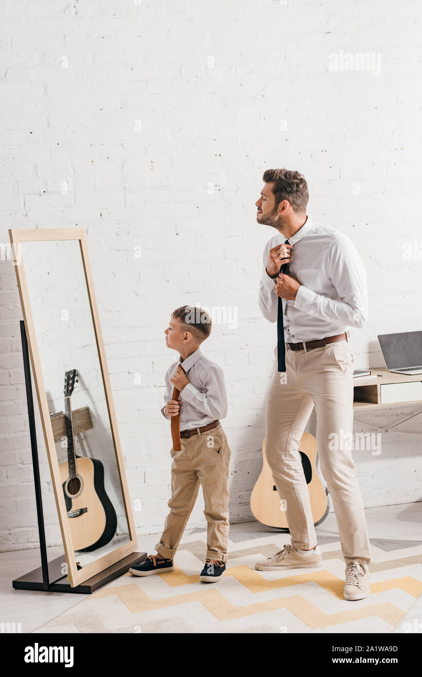 full length view of son and father in formal wear standing near mirror ...