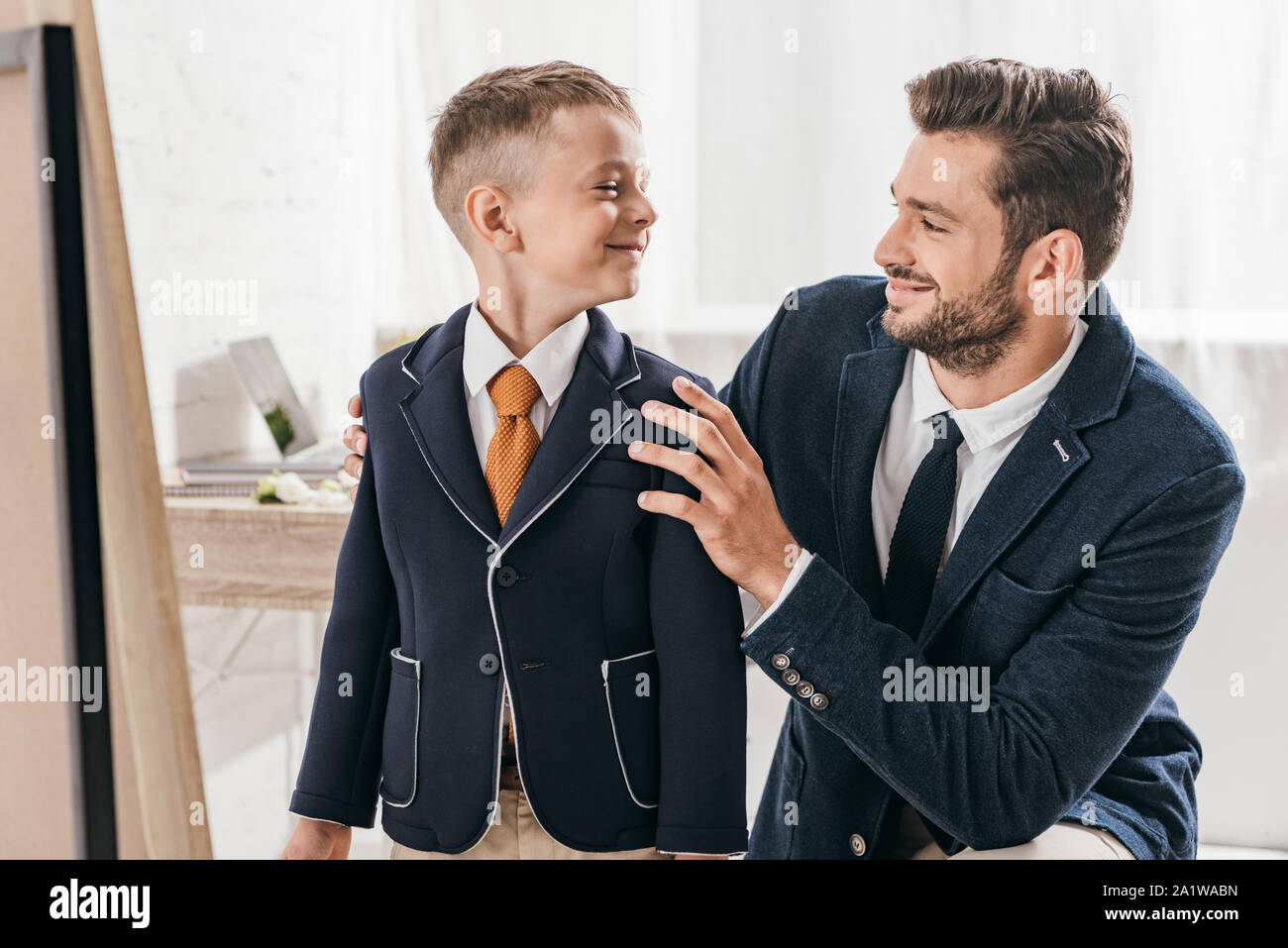 confident dad and son in formal wear looking at each other at home ...