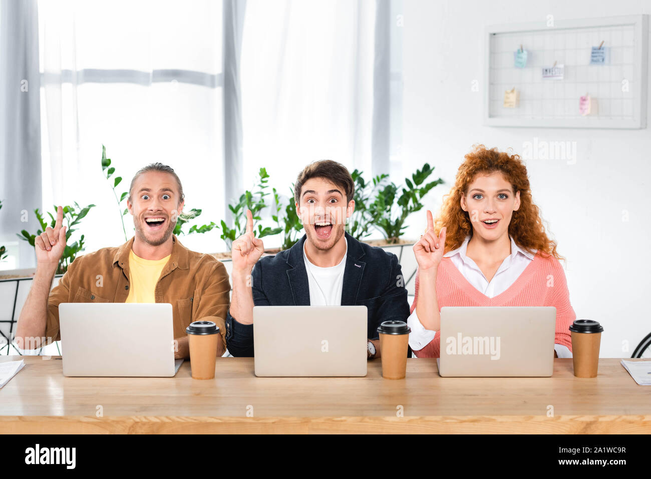 three shocked friends sitting at table and showing idea signs Stock ...