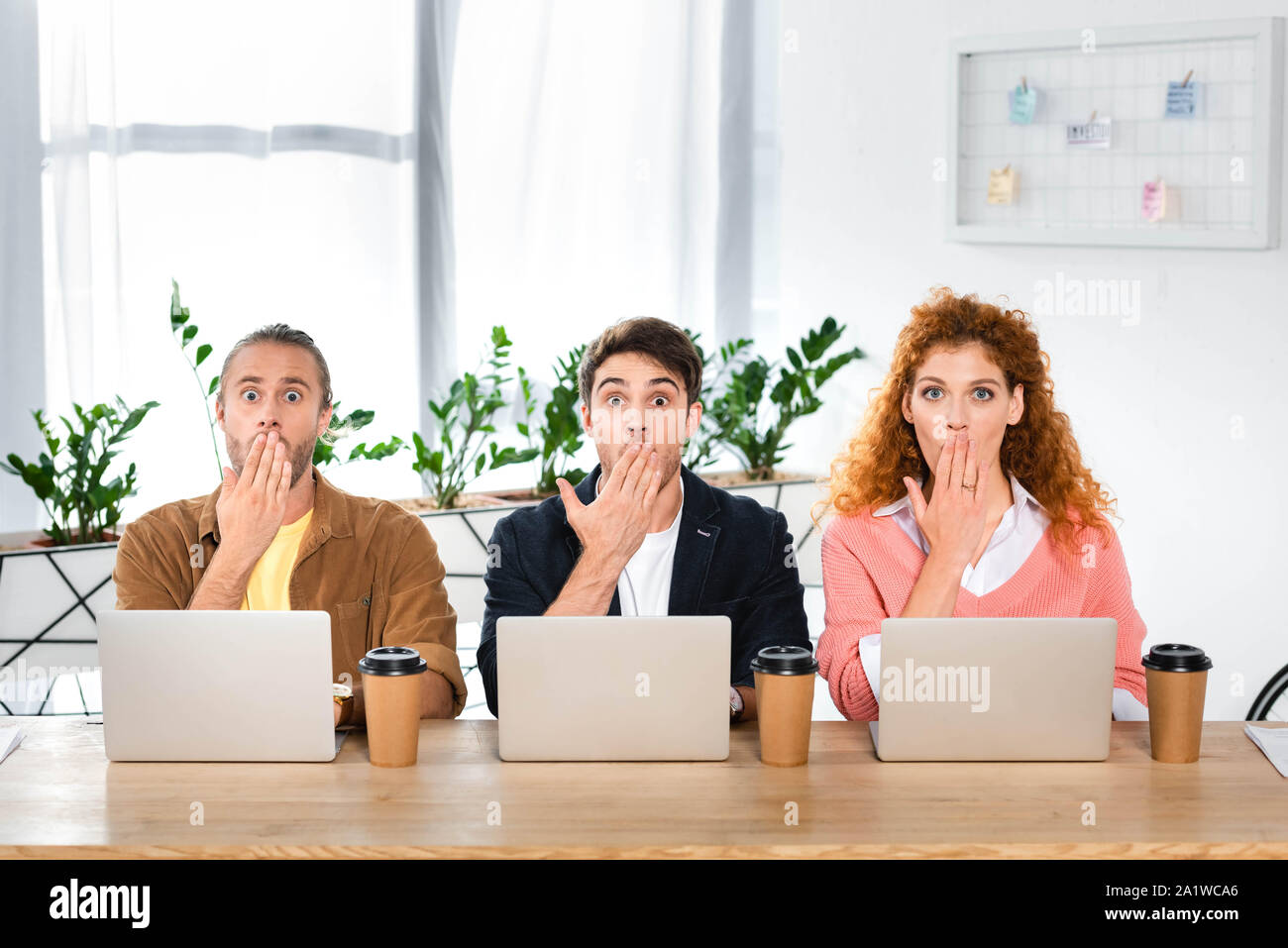 three shocked friends sitting at table and obscuring faces Stock Photo ...