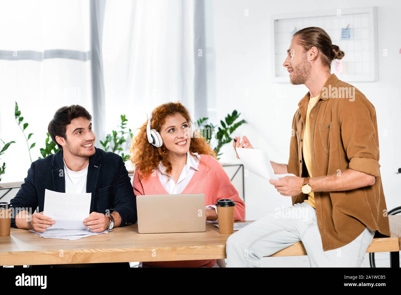 three smiling friends holding papers and talking in office Stock Photo ...