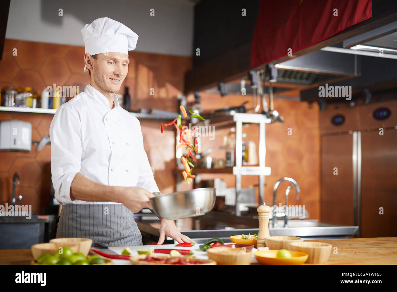 Waist up portrait of handsome chef tossing vegetable while cooking ...