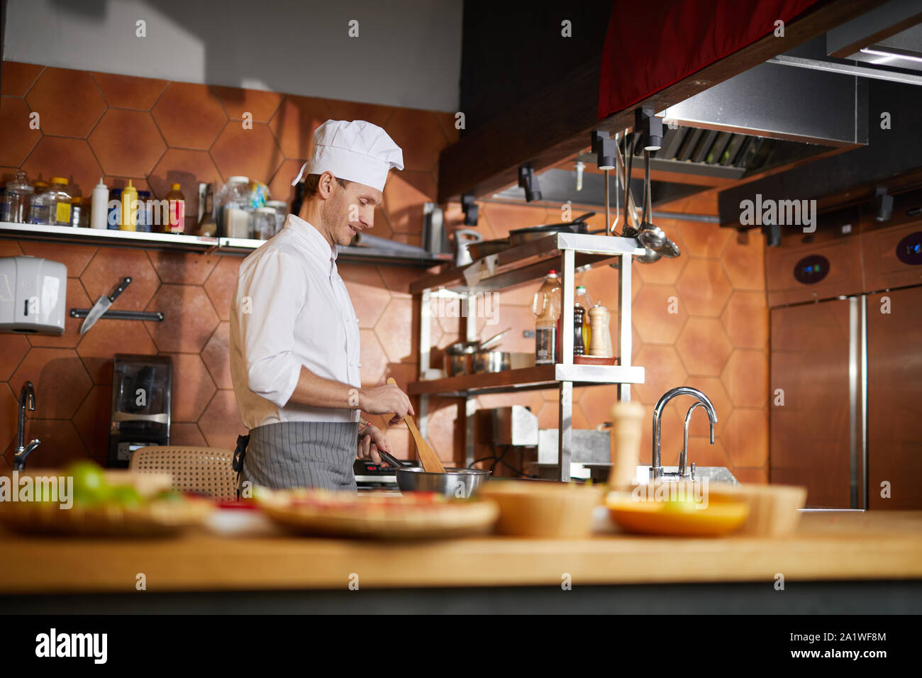 Side view portrait of handsome chef cooking dishes in frying pan while ...