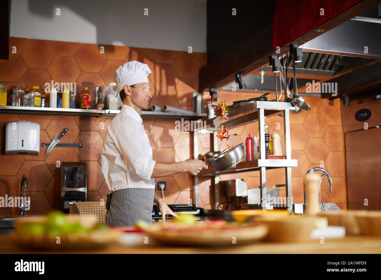 Side view portrait of handsome chef tossing vegetable while cooking ...