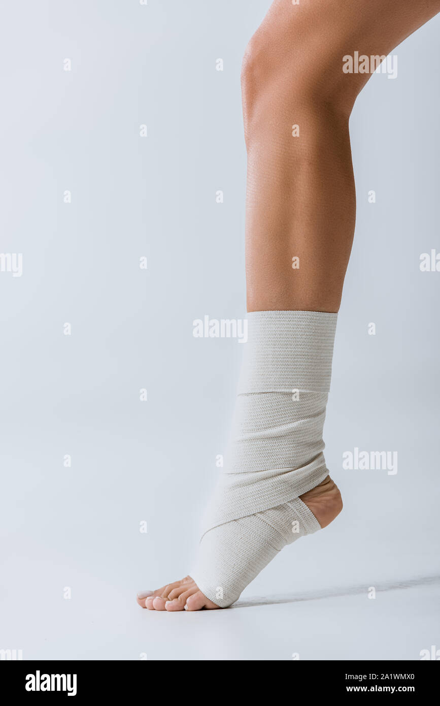 partial view of barefoot girl with elastic bandage on foot on grey ...