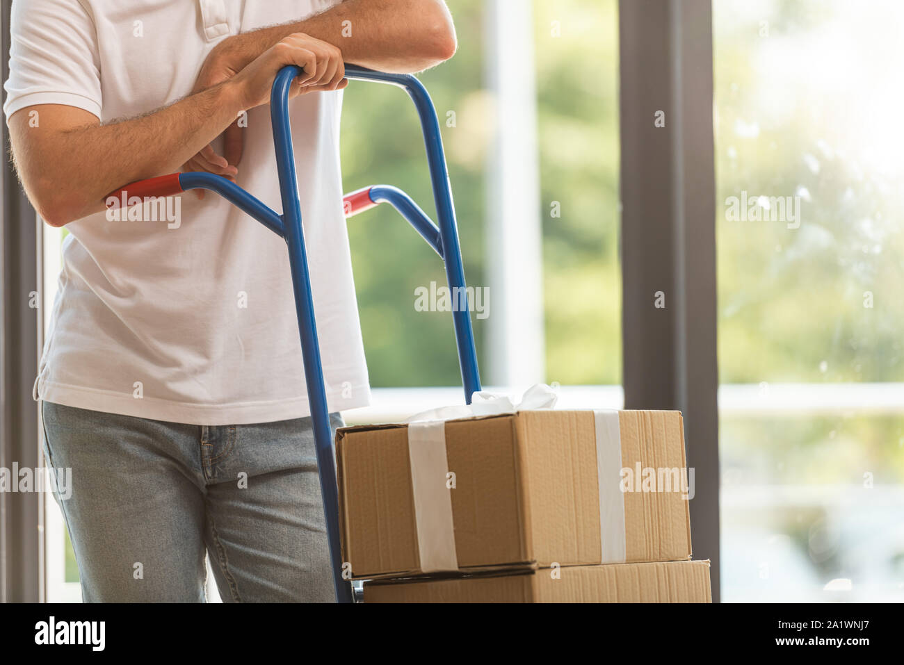 cropped view of delivery man standing near delivery cart with cardboard ...