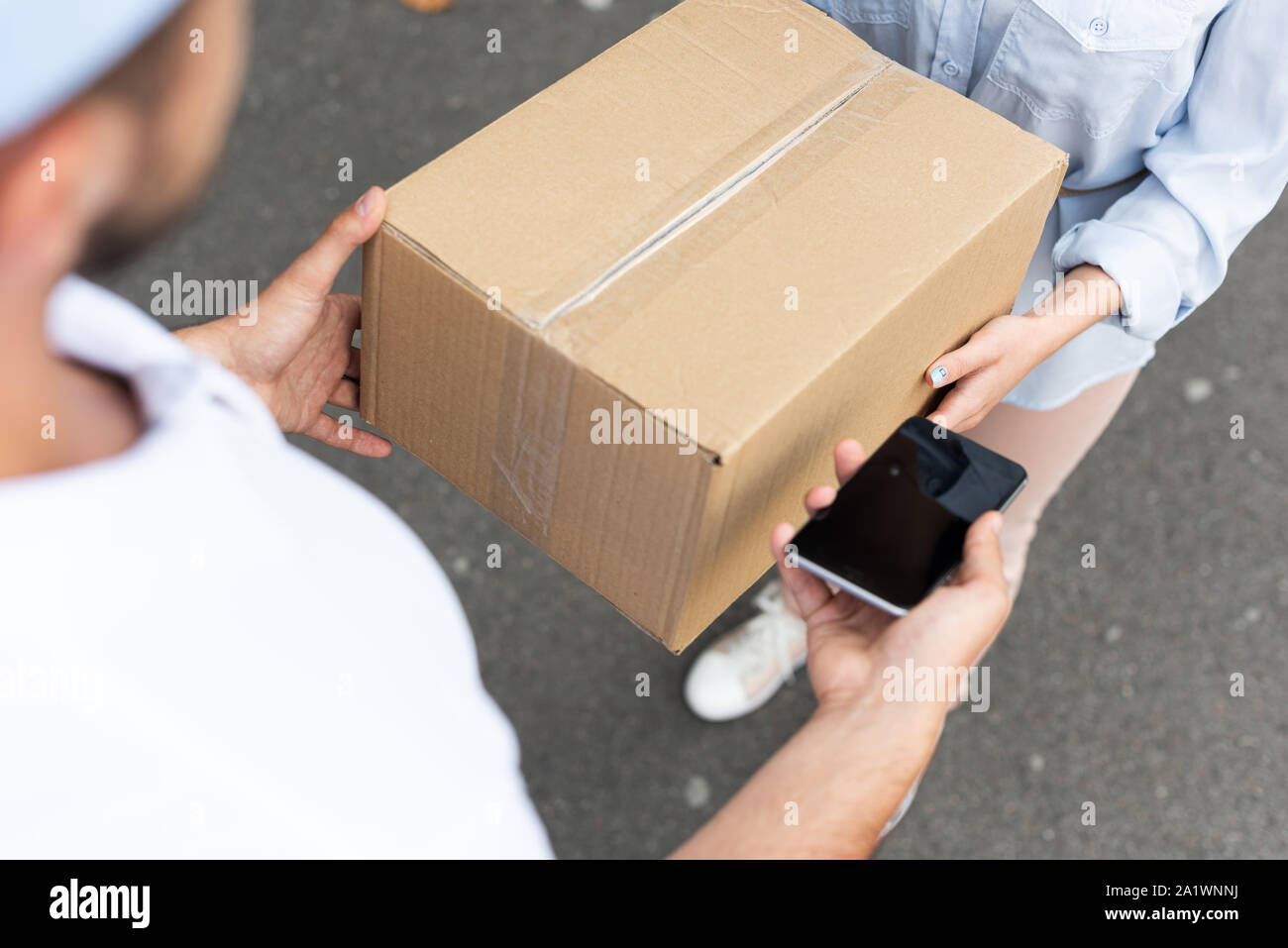 overhead view of delivery man giving box to woman while taking ...