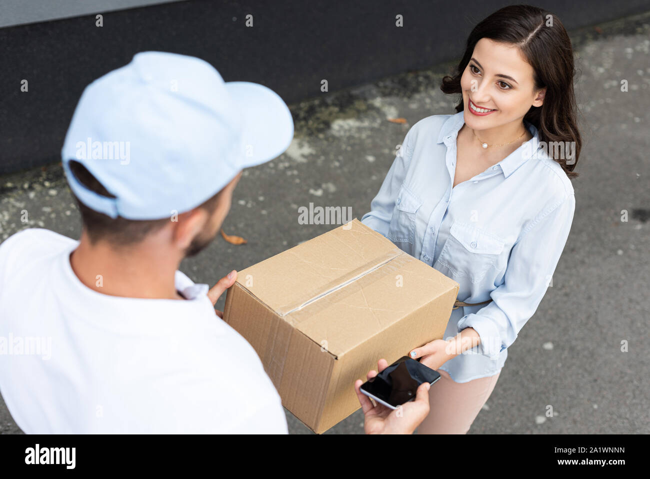overhead view of delivery man in cap giving box to happy woman while ...