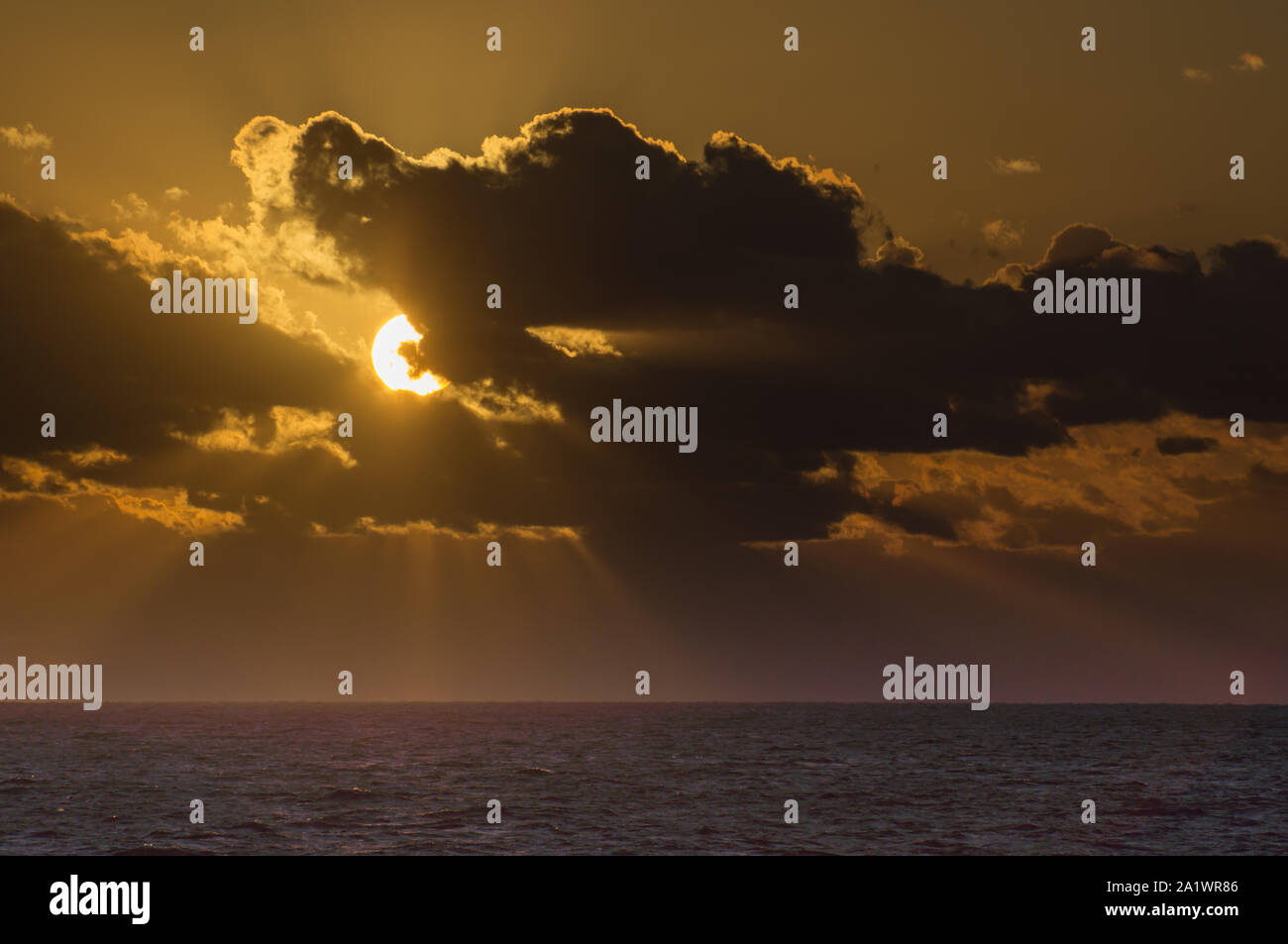 Setting sun hides behind the clouds over a dark purple Caribbean Sea ...