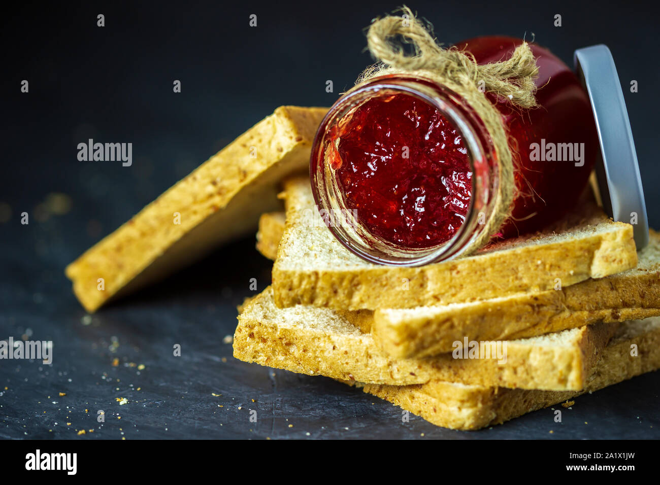 Strawberry jam bottle and whole wheat bread are stacked on a black ...