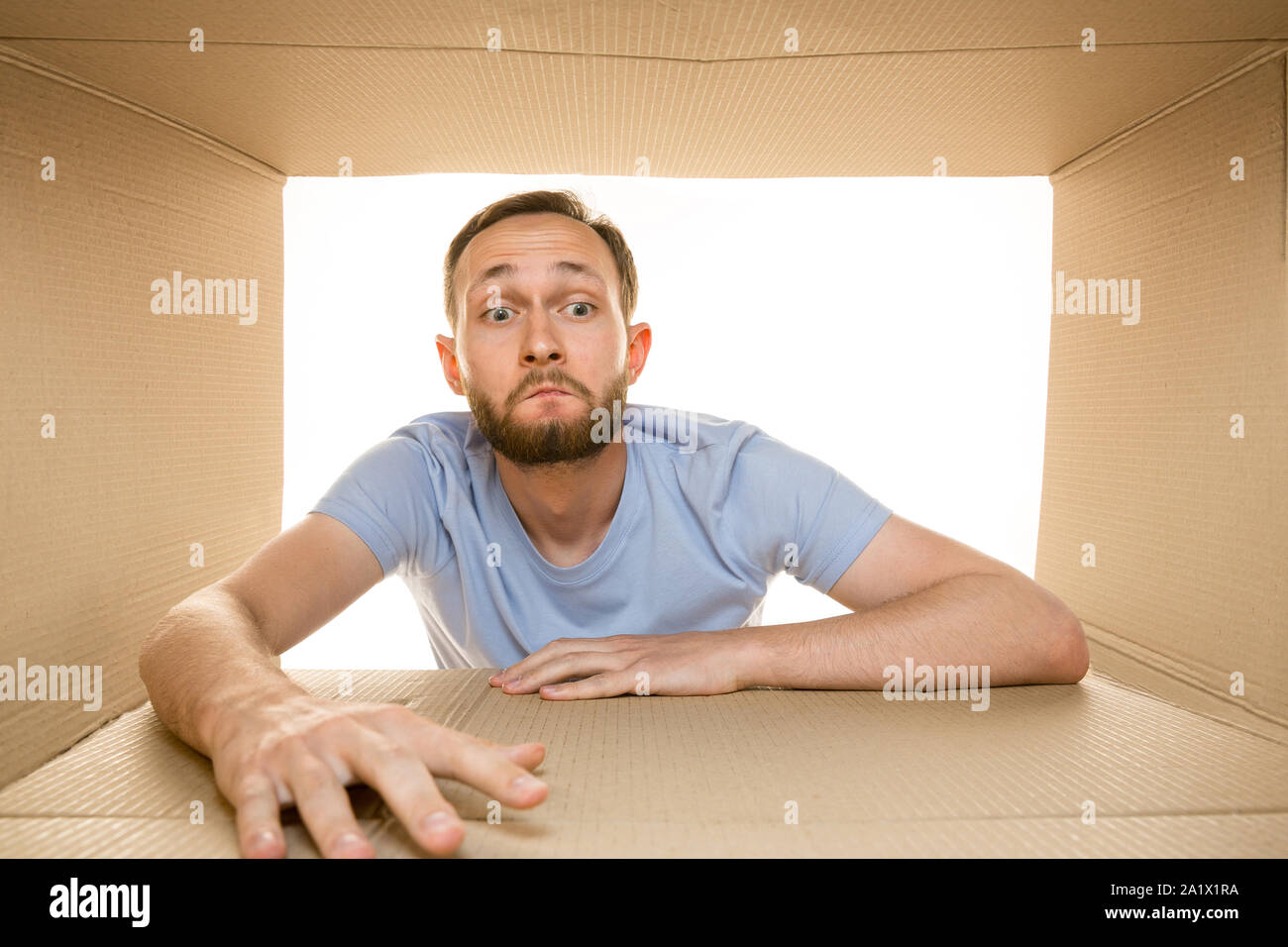 Young sad man opening the biggest postal package isolated on white ...