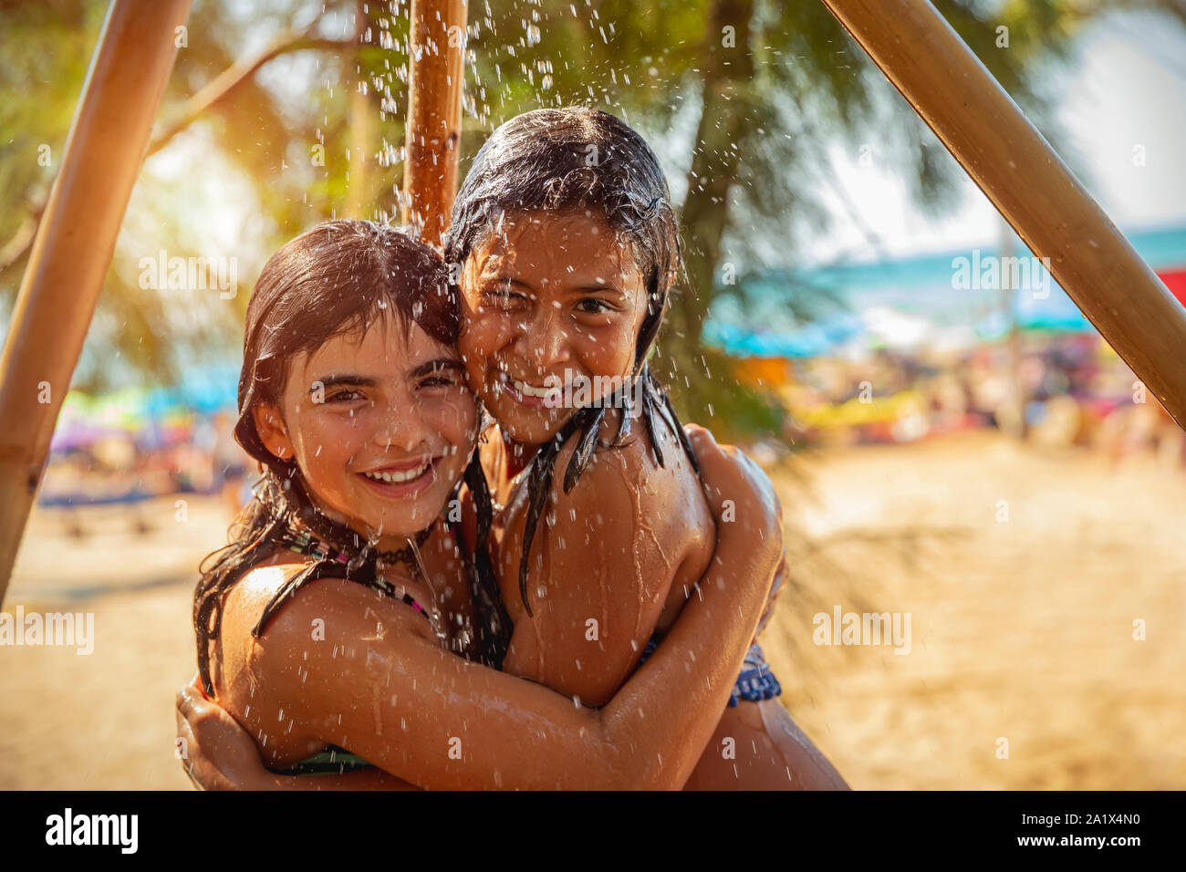 Portrait of a two little girls standing together under outdoor shower on the beach, best friends ...