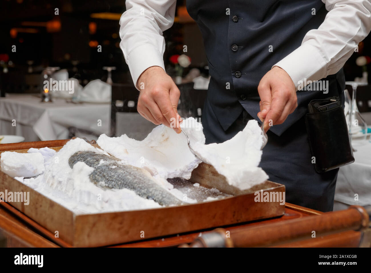 Waiter is carving fish baked in salt crust by restaurant table Stock ...