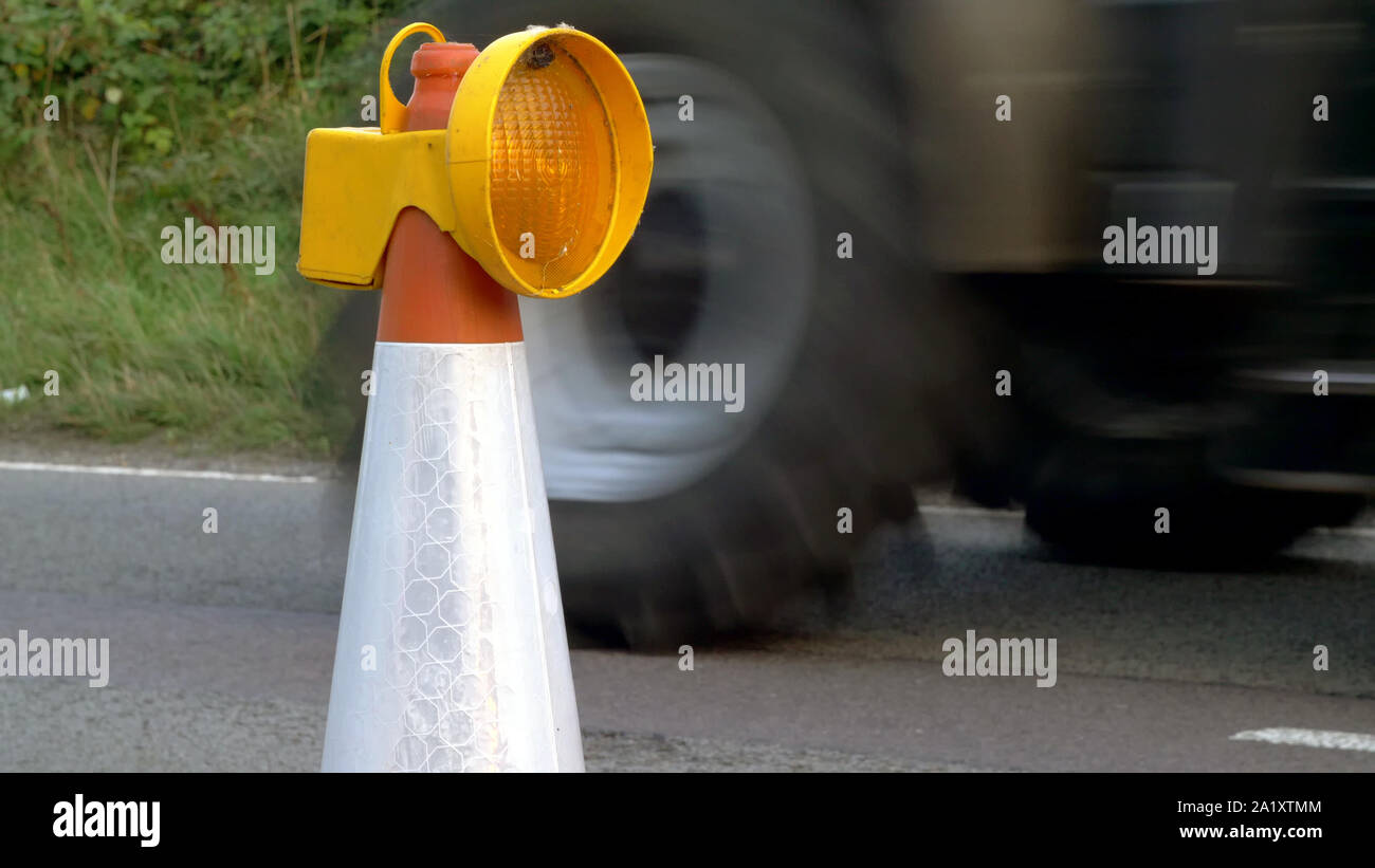 roadworks cone flashing on UK motorway at evening with traffic passing ...