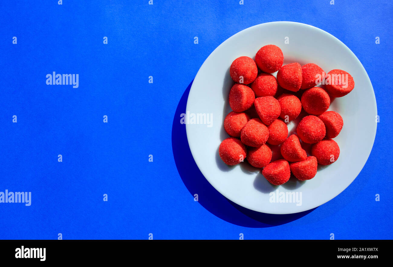 Red strawberry sugary candies in white plate on blue background with ...