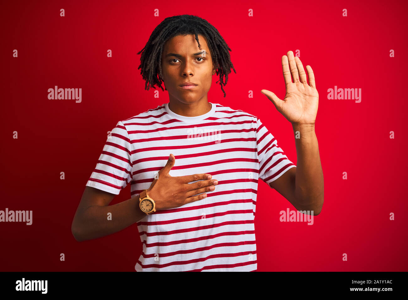 Young afro man with dreadlocks wearing striped t-shirt standing over ...