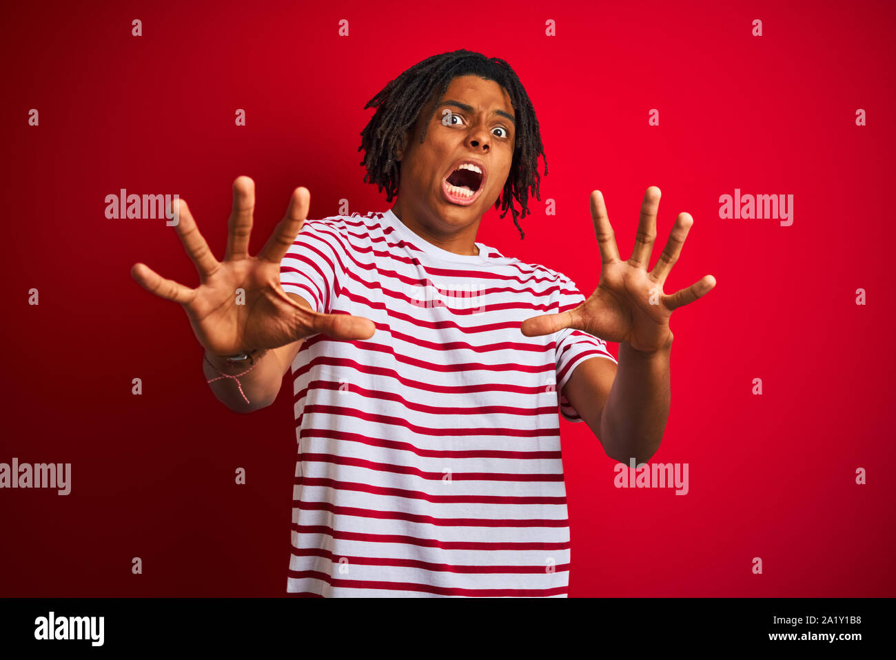 Young afro man with dreadlocks wearing striped t-shirt standing over ...