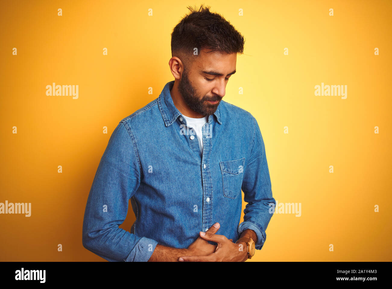 Young indian man wearing denim shirt standing over isolated yellow ...