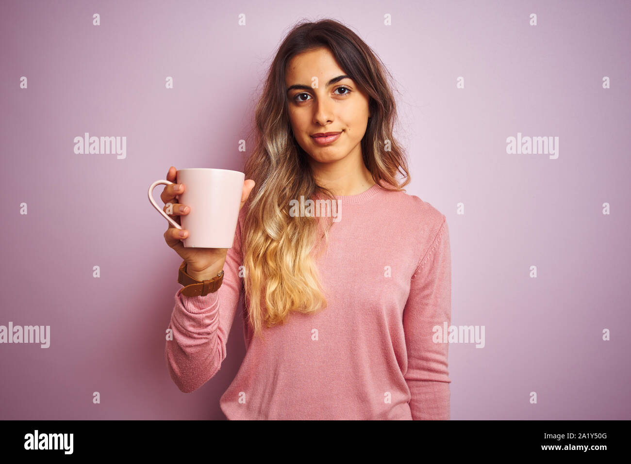 Young beautiful woman holding cup of coffee over pink isolated ...