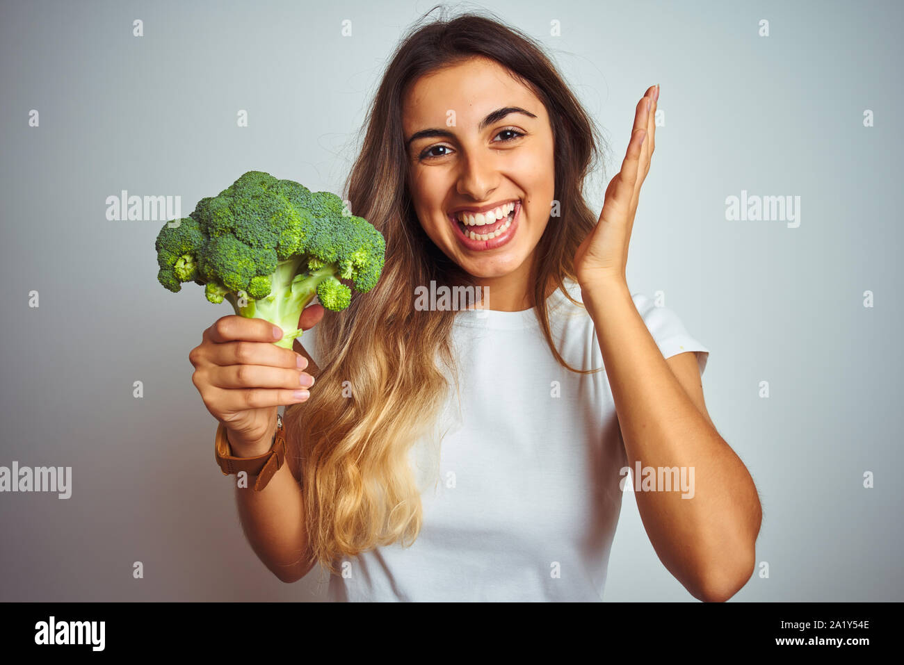Young beautiful woman eating broccoli over grey isolated background ...