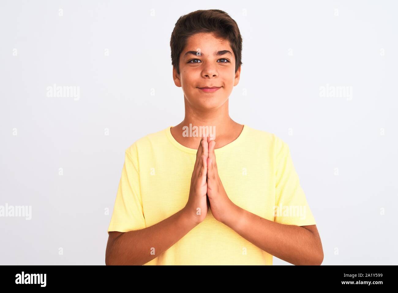 Handsome teenager boy standing over white isolated background praying ...