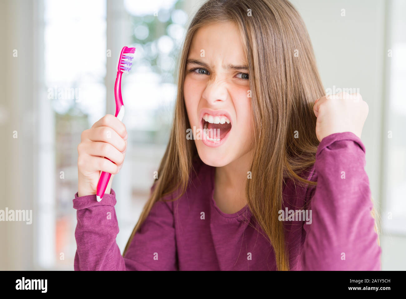 Beautiful young girl kid holding pink dental toothbrush annoyed and ...