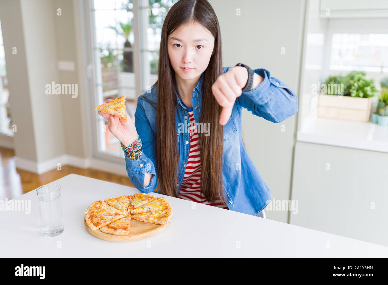 Beautiful Asian woman eating a slice of cheese pizza with angry face ...