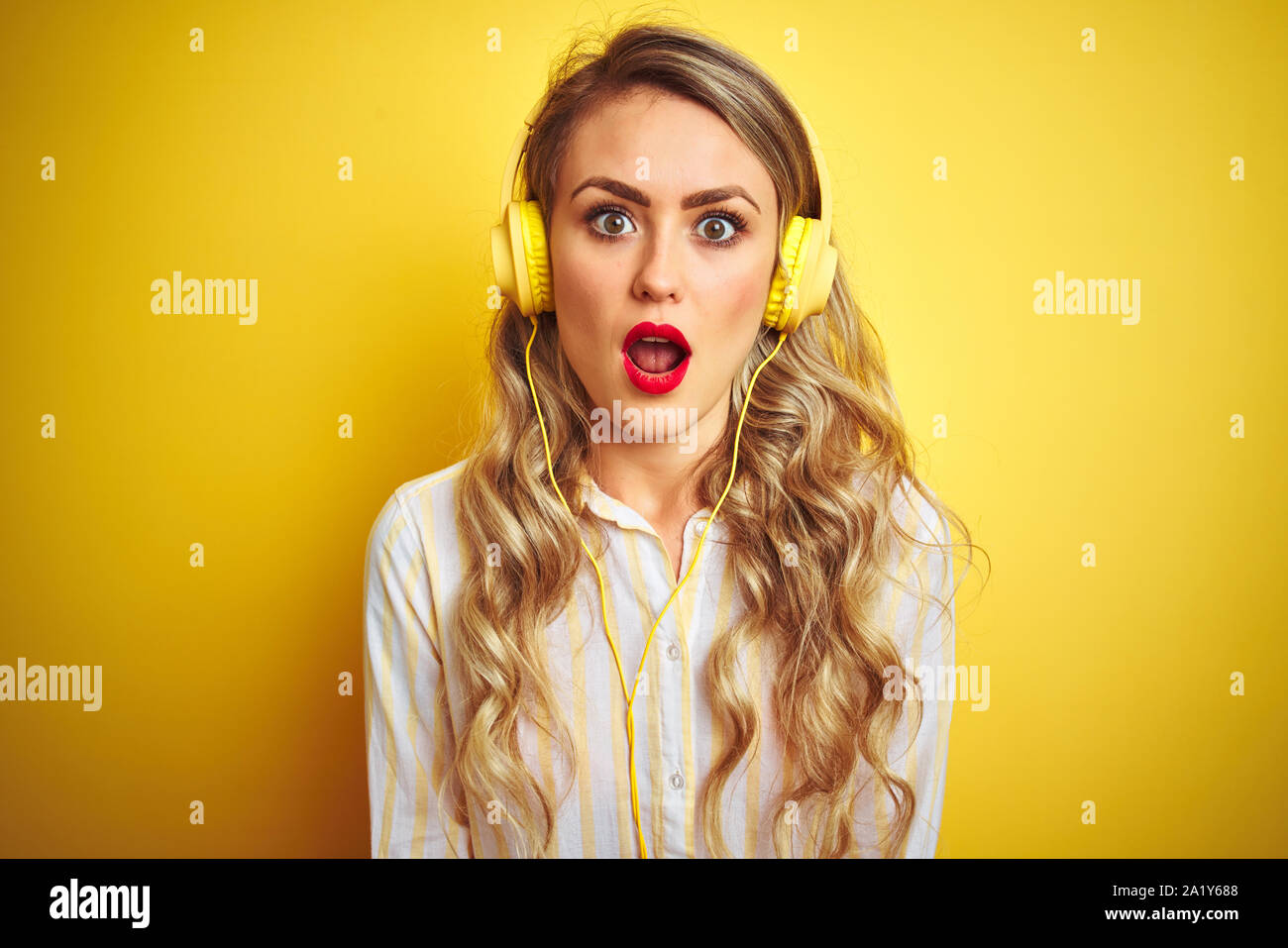 Young beautiful woman listening to music using headphones over yellow ...