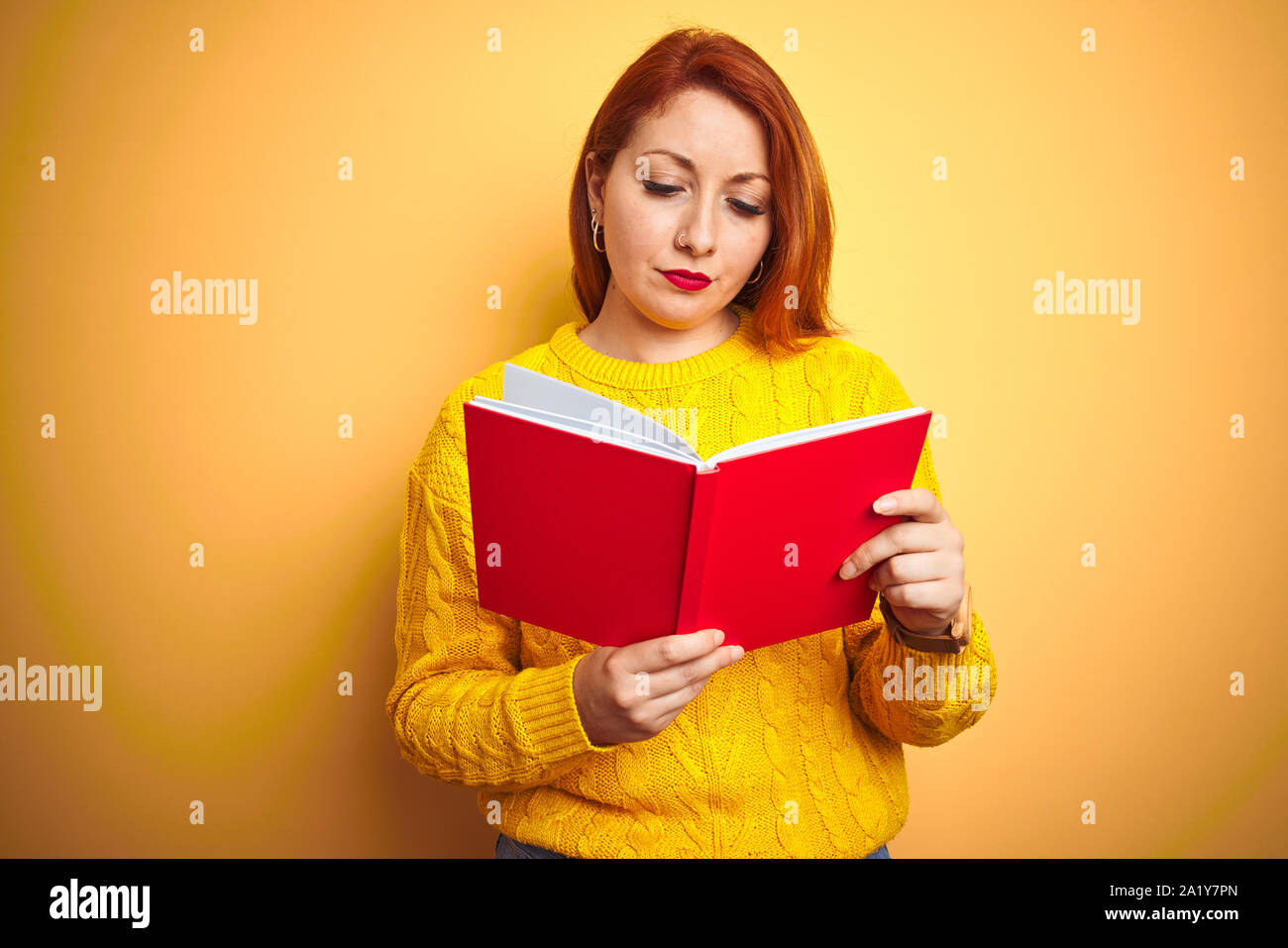 Young redhead teacher woman reading red book over yellow isolated ...