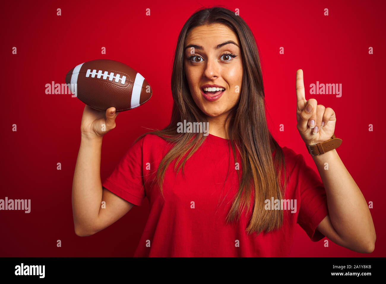 Young beautiful sportswoman holding football ball over isolated red ...
