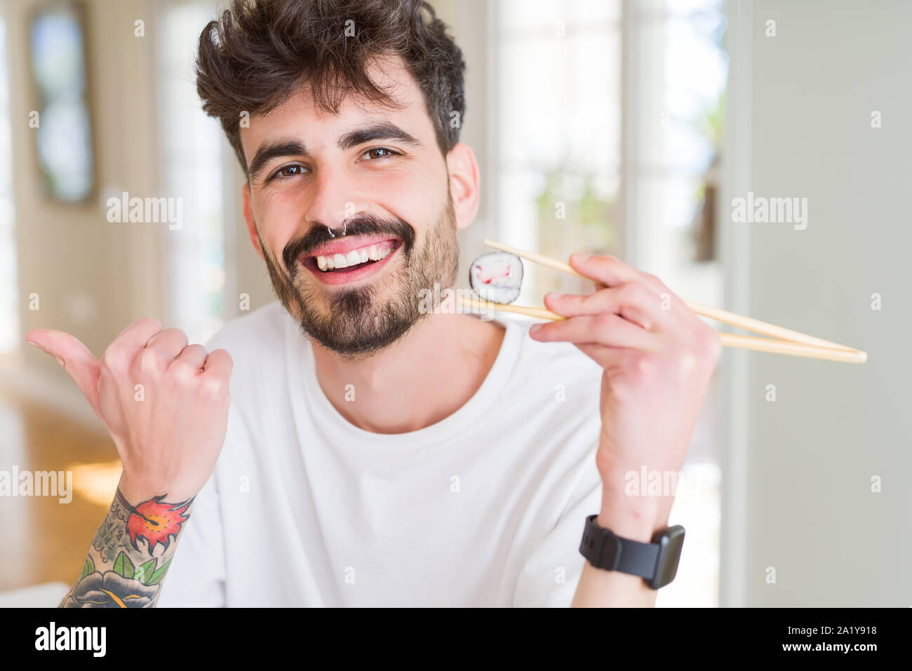 Young man eating asian sushi using chopsticks pointing and showing with ...