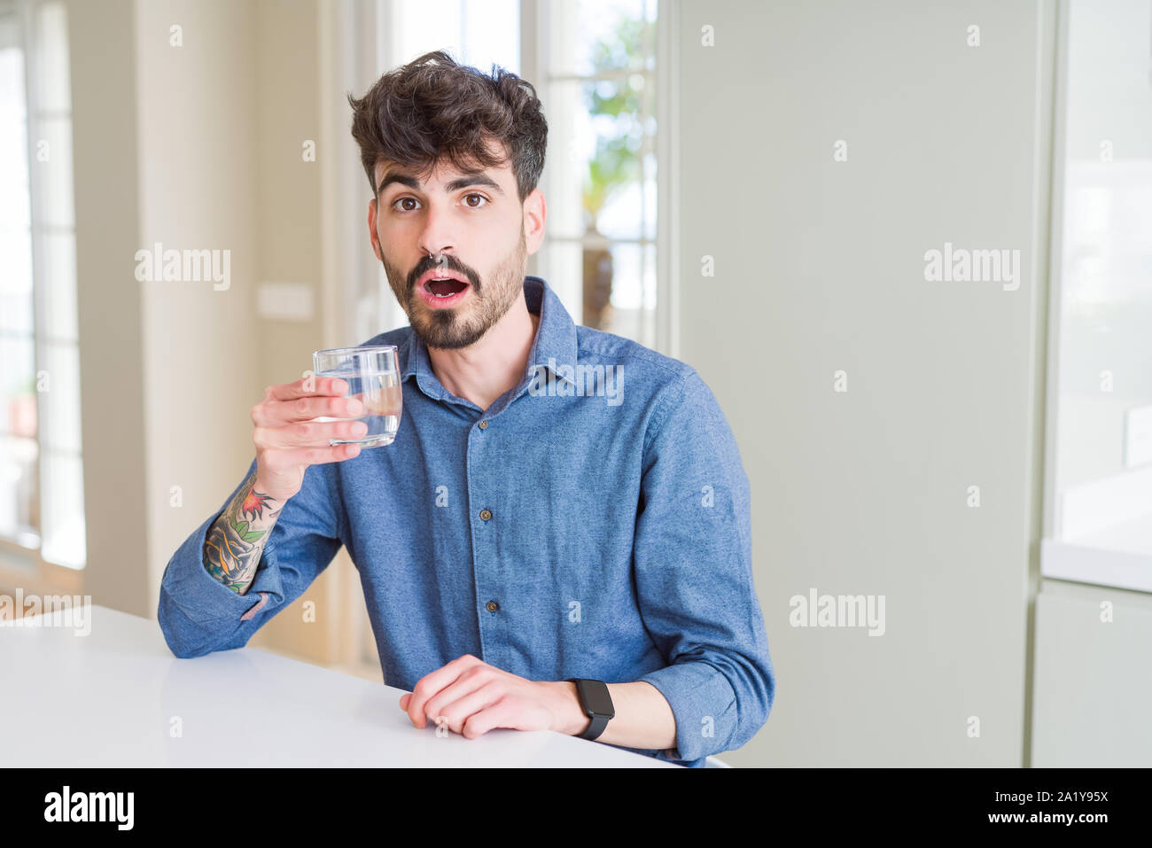 Young man drinking a fresh glass of water scared in shock with a ...