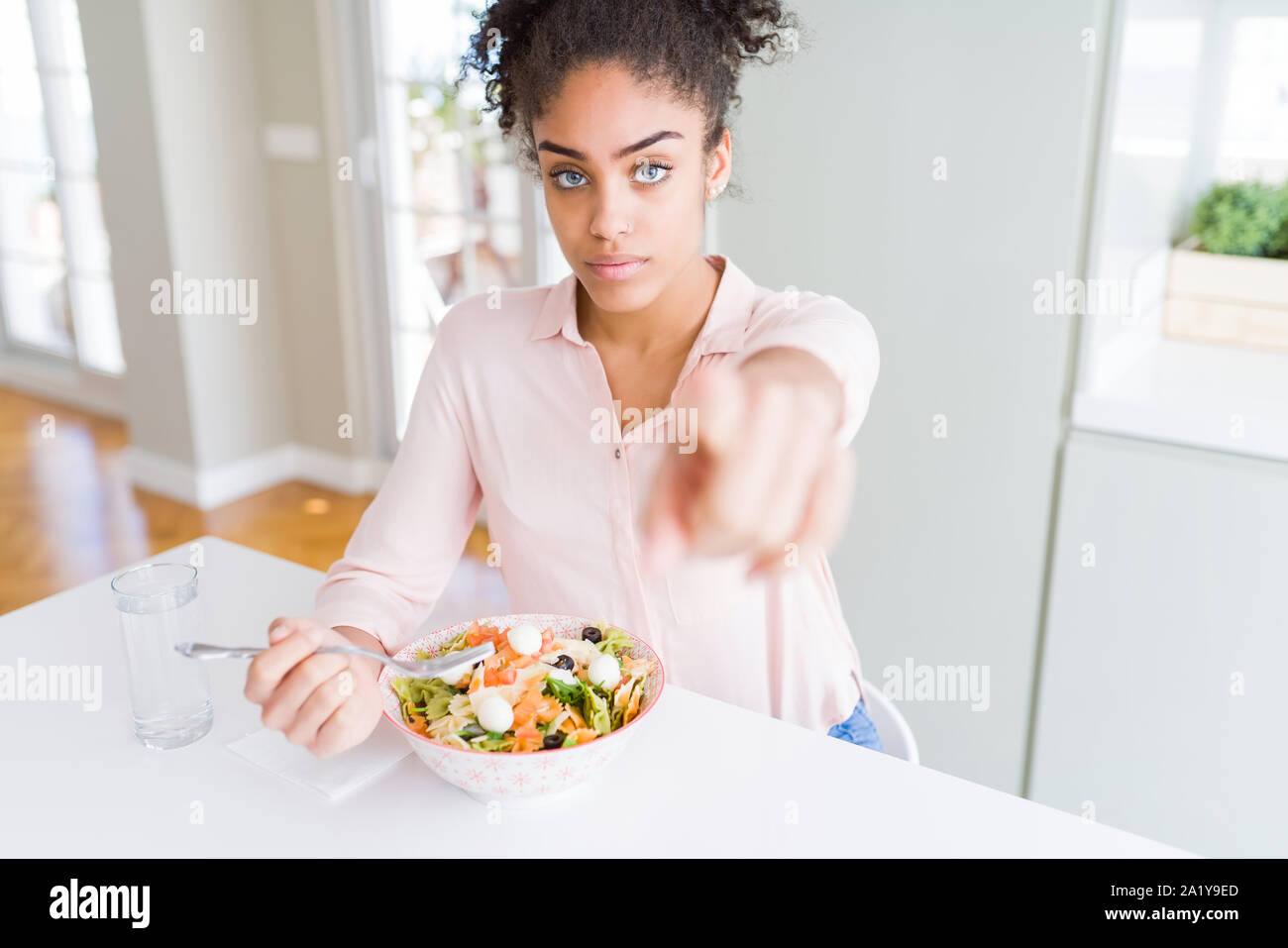 Young african american woman eating healthy pasta salad pointing with ...