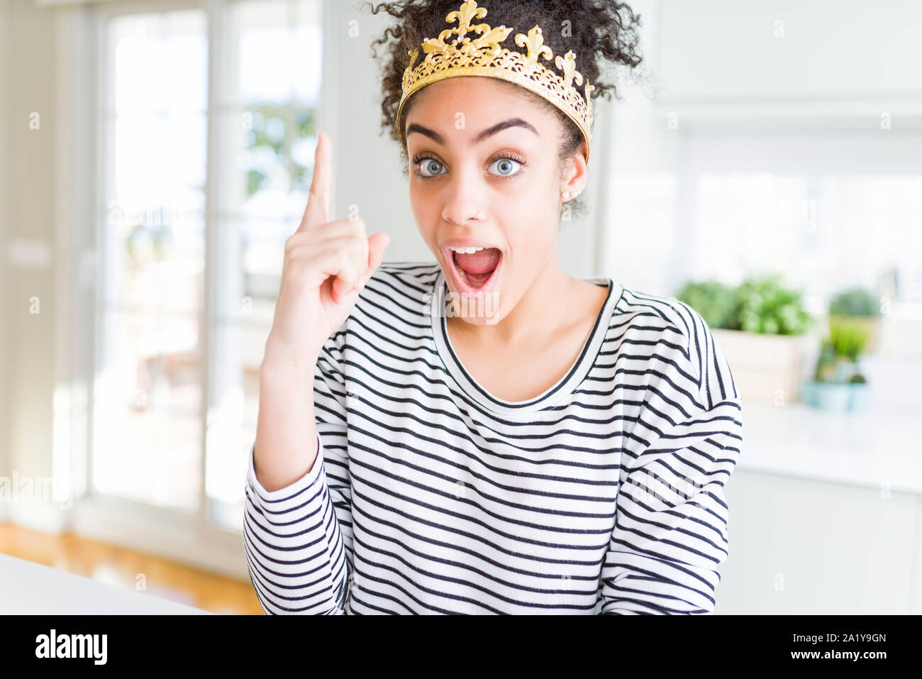 Young african american girl wearing golden queen crown on head pointing ...