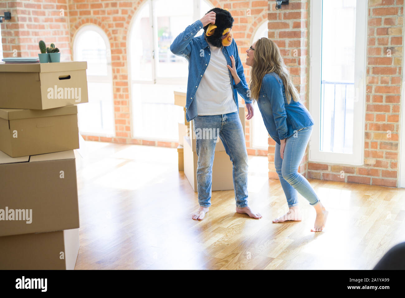 Young couple having fun wearing a monkey mask moving to a new apartment ...
