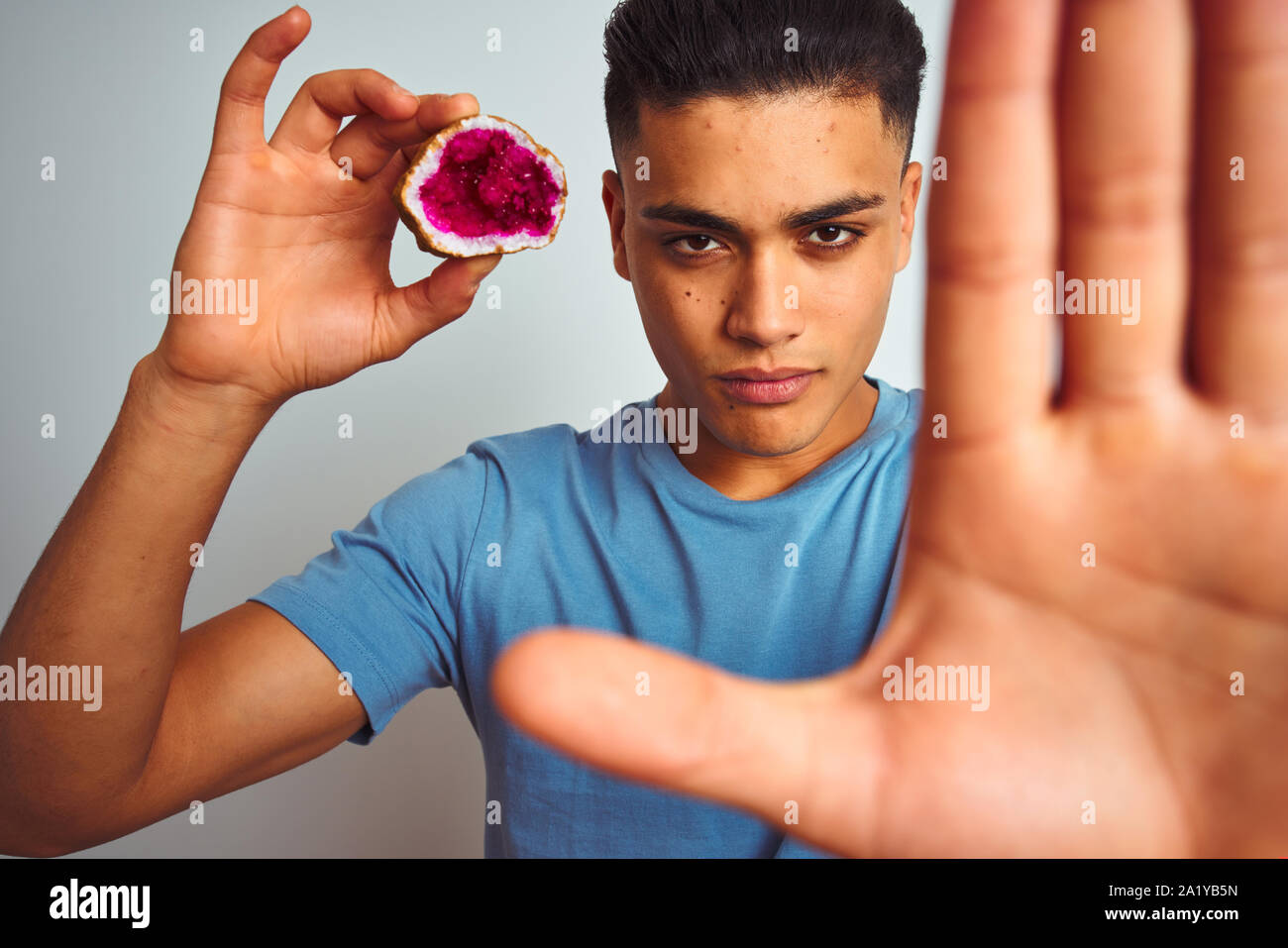 Young brazilian man holding amethyst gemstone standing over isolated ...