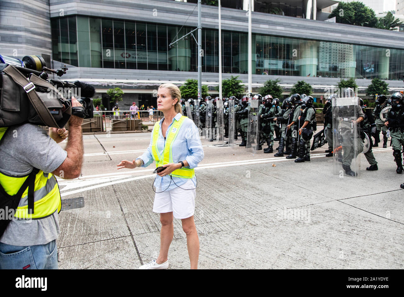 A TV reporter broadcasting in front of riot police during the ...