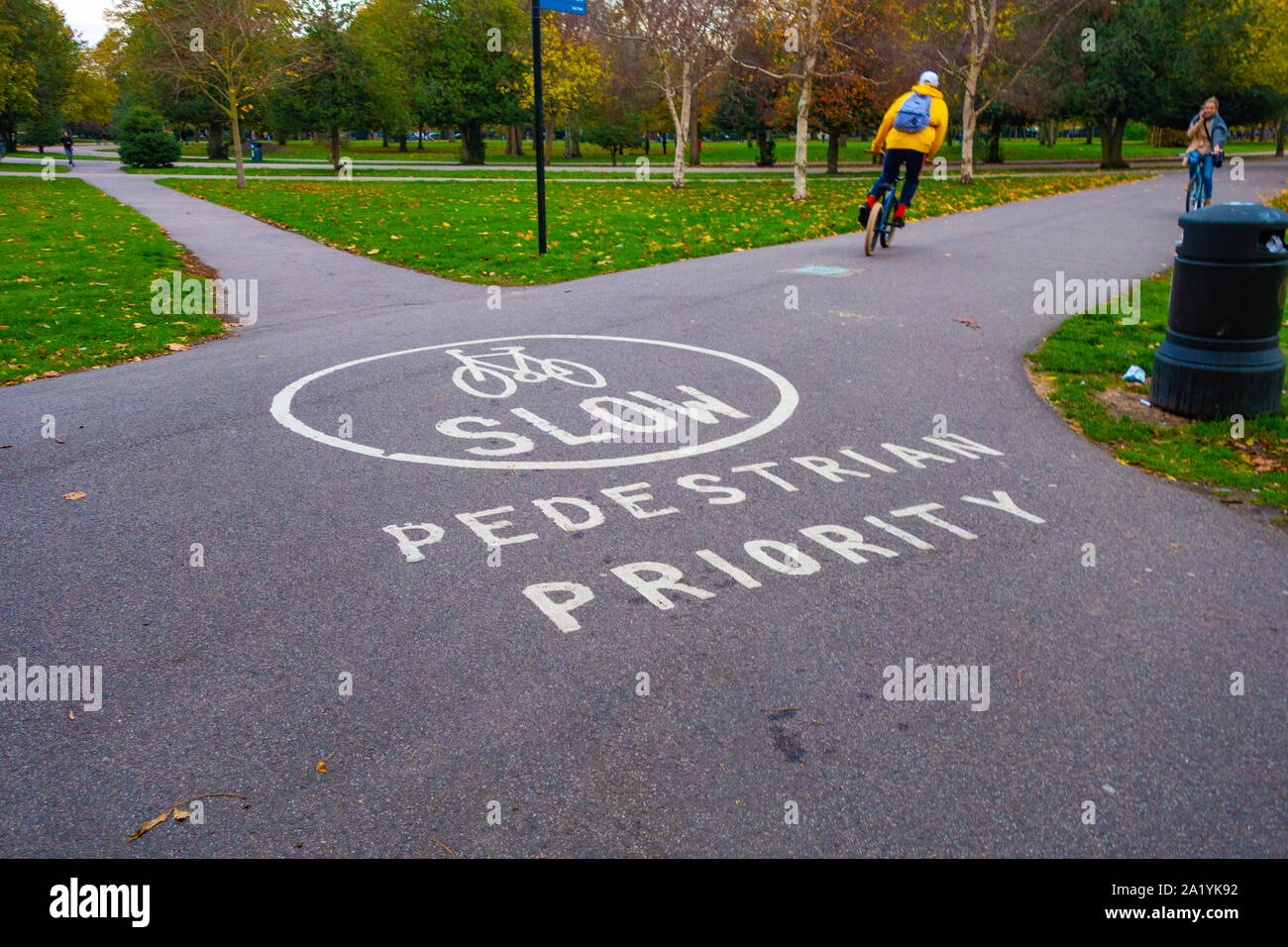 Cyclist riding over a pedestrian priority warning sign on a park ...