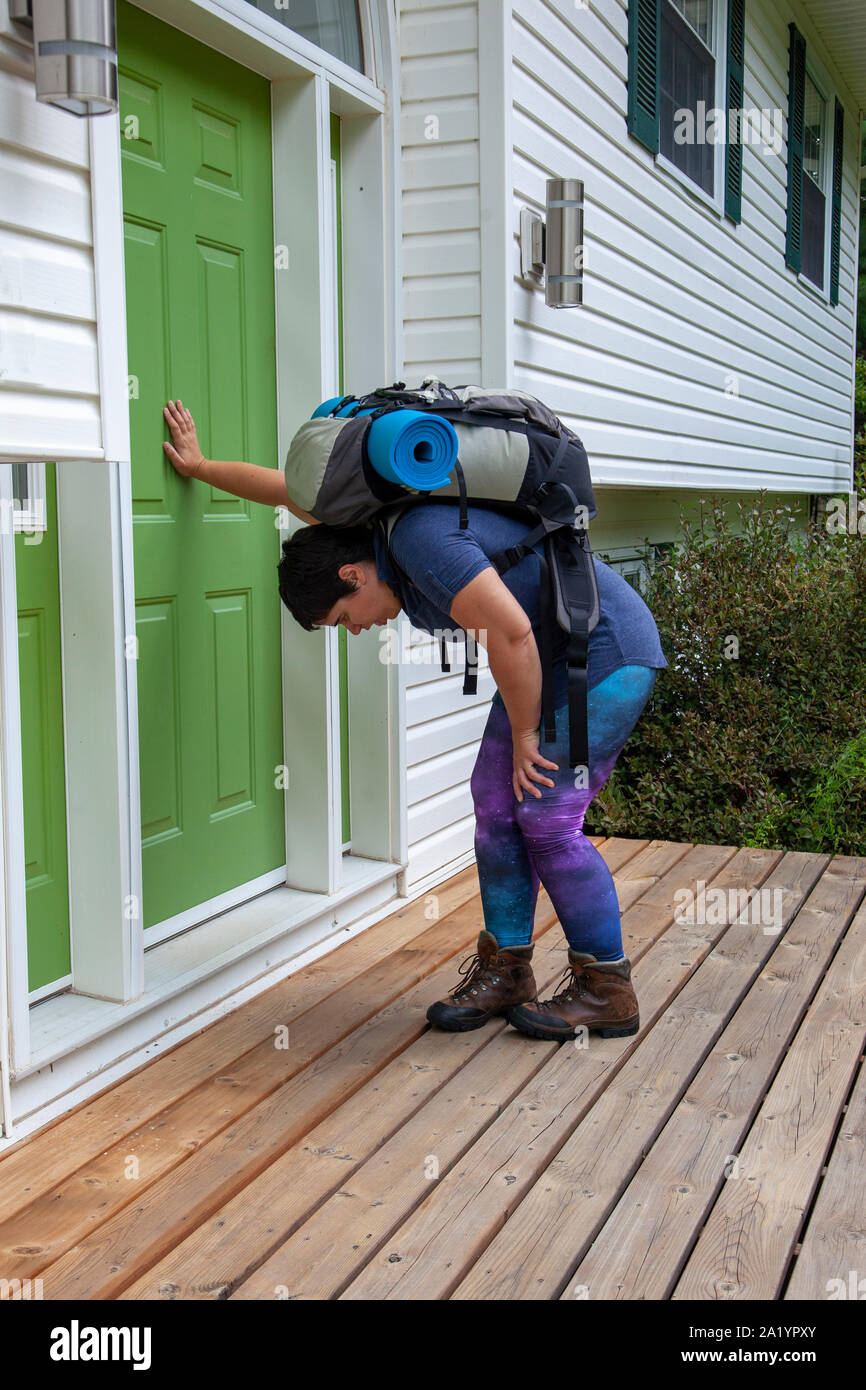 person leaning against their front door with backpack and camping roll ...