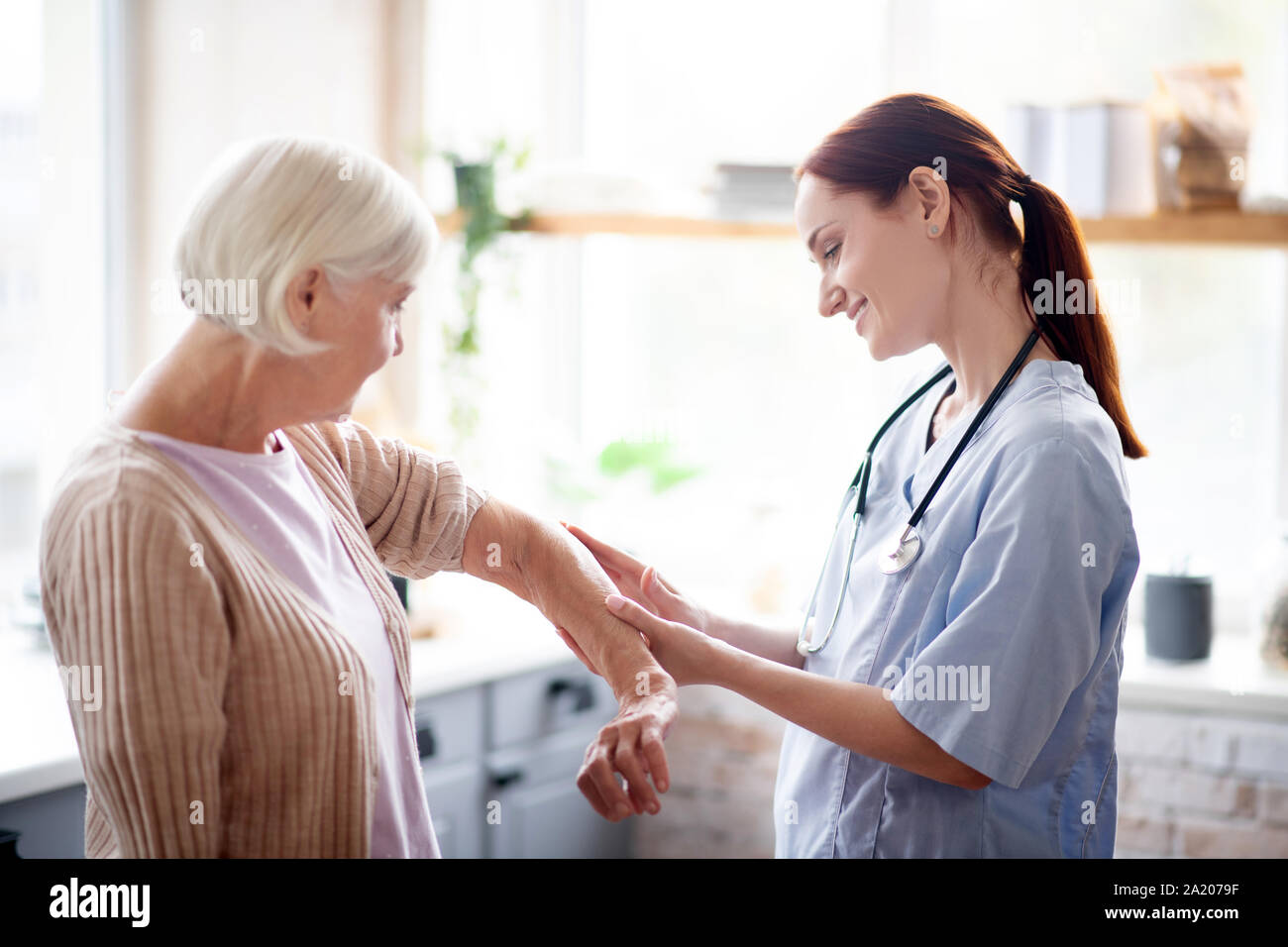 Caregiver putting gel on elbow of retired woman Stock Photo - Alamy