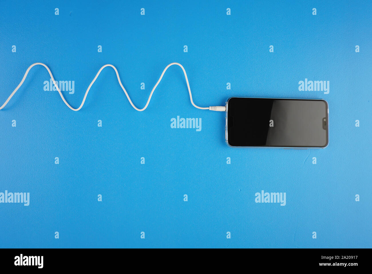 Wave shape of white cable attached on smartphone over blue background ...