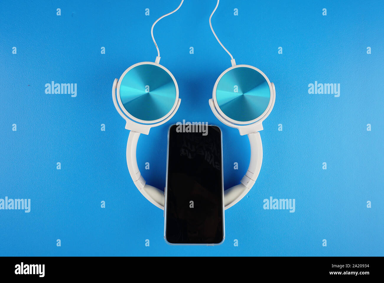 blue white color headphone placed next to handphone on a blue ...