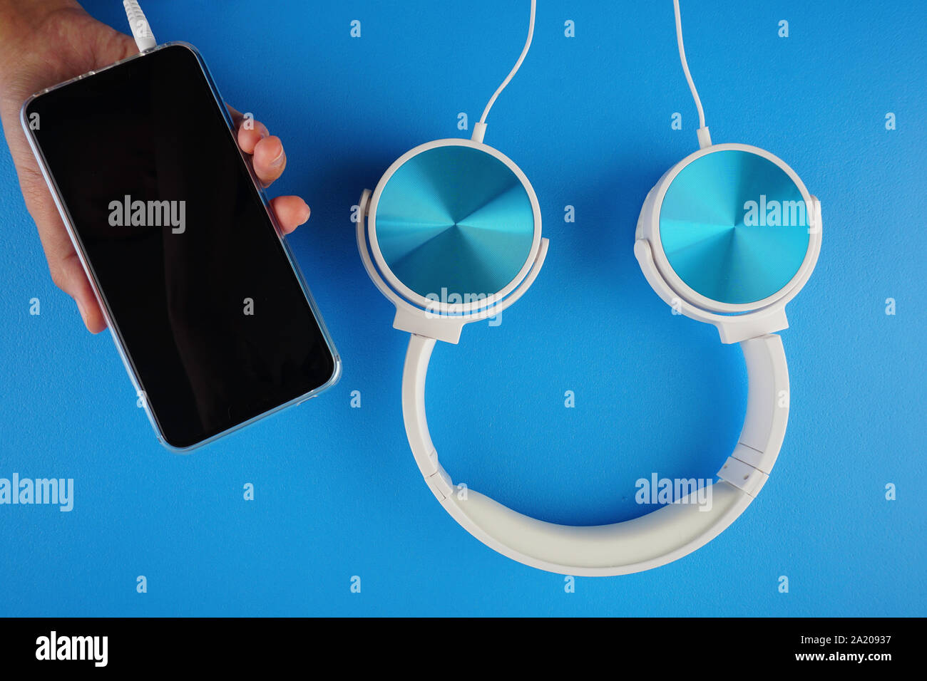 A hand holding a handphone with blue white color headphone on a blue ...