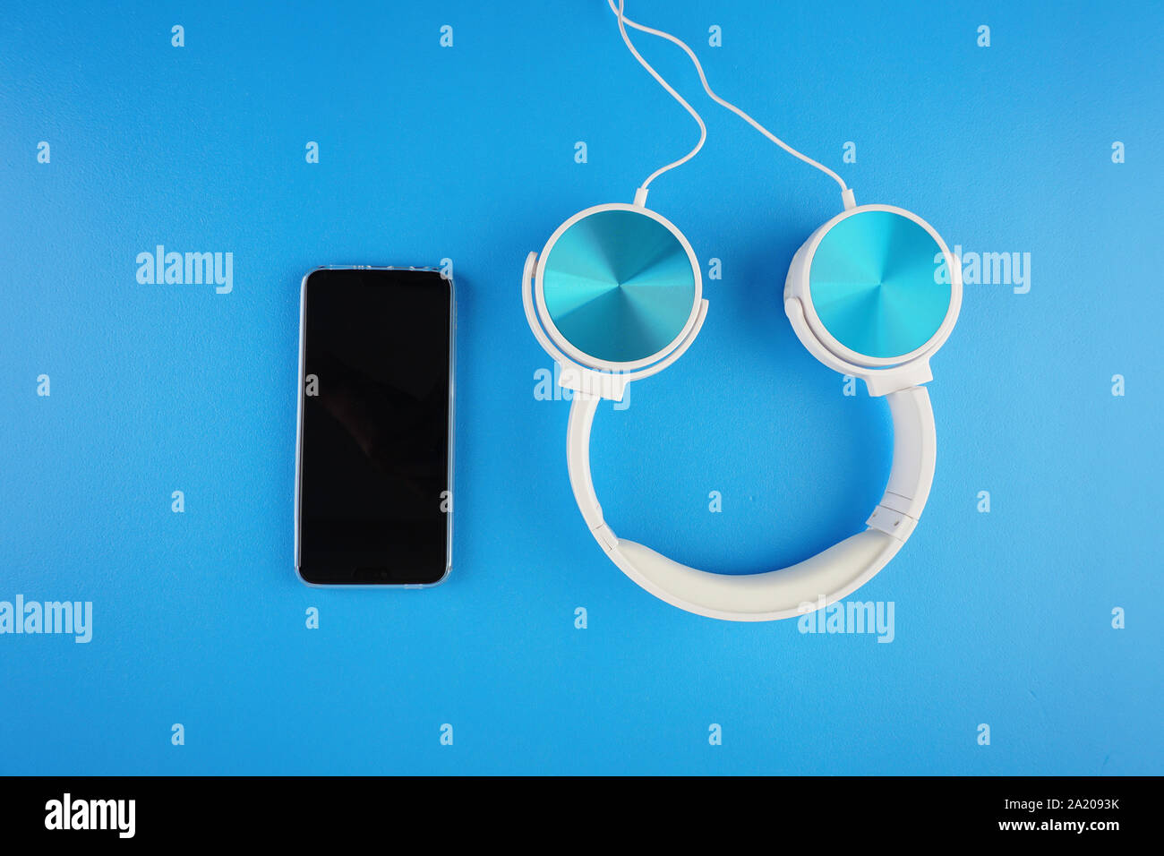 blue white color headphone placed next to handphone on a blue ...